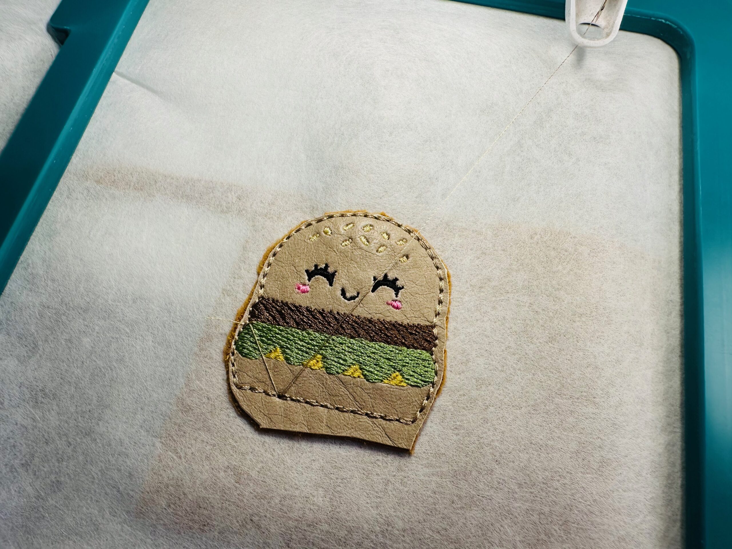 A cute hamburger patch with a smiling face on a white surface. - Sulky