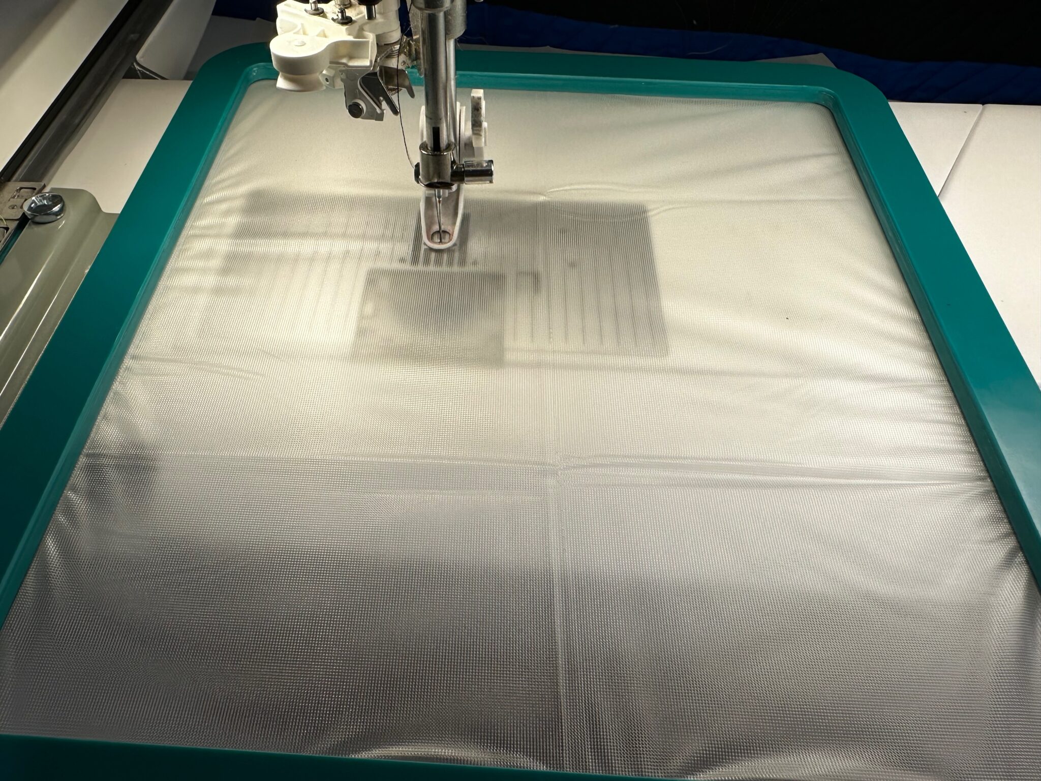 A sewing machine stitching a square pattern on white fabric. - Sulky
