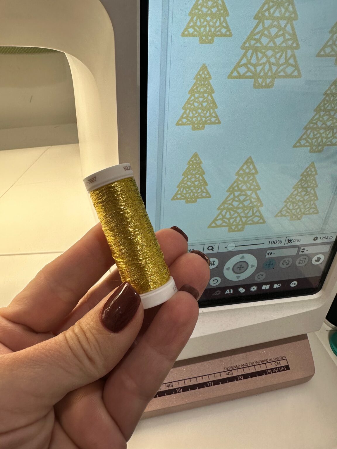Hand holding spool of gold thread in front of a sewing machine. - Sulky